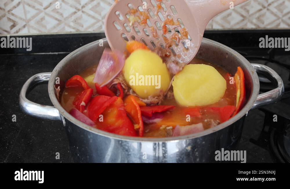 Chef stirring a bubbling stew in a pot on the stove with a skimmer ...