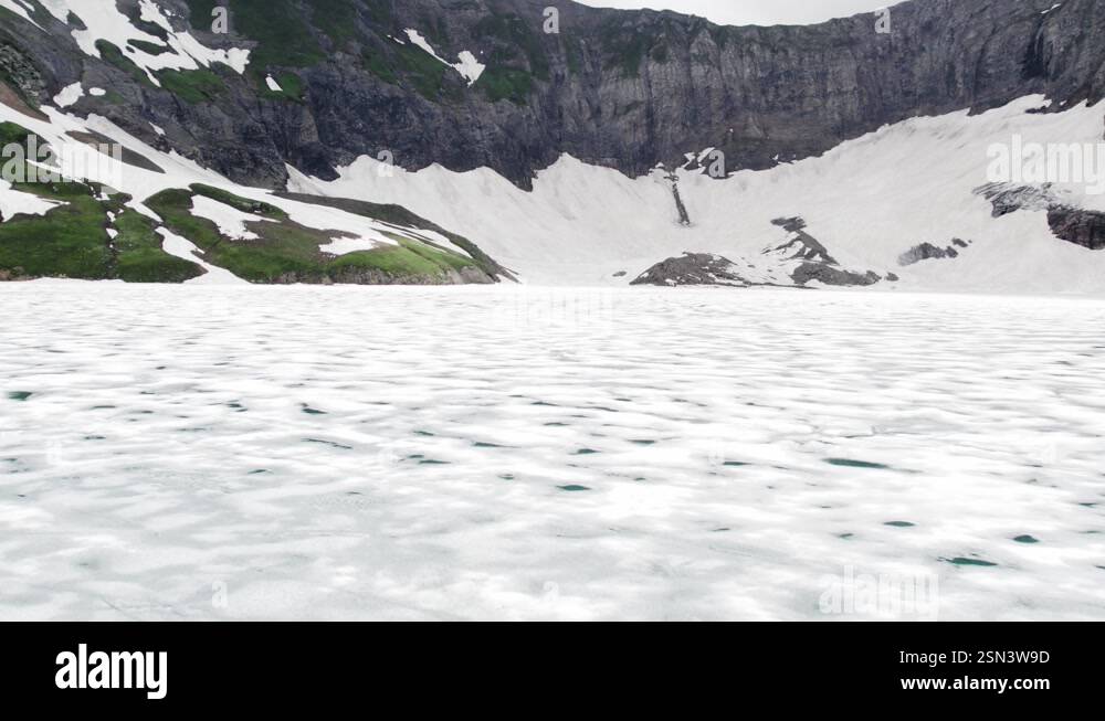 A frozen alpine lake with patches of snow and rocky cliffs Stock Video ...