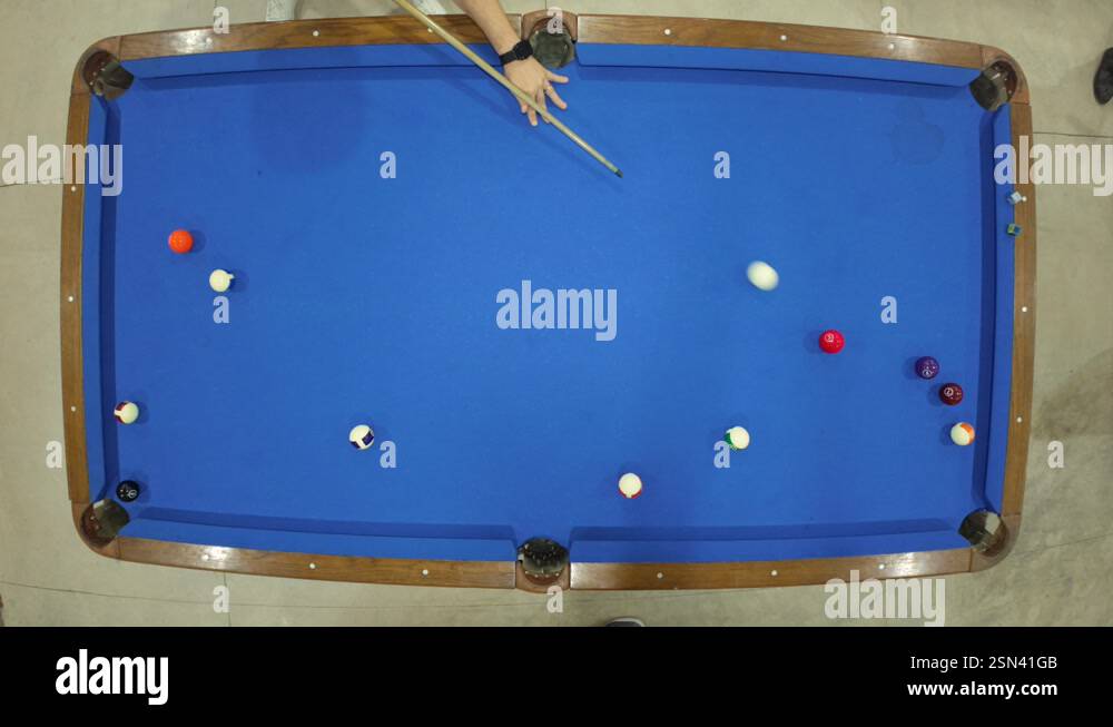 Top-down view of a blue billiards table as a man aims and hits the ball ...
