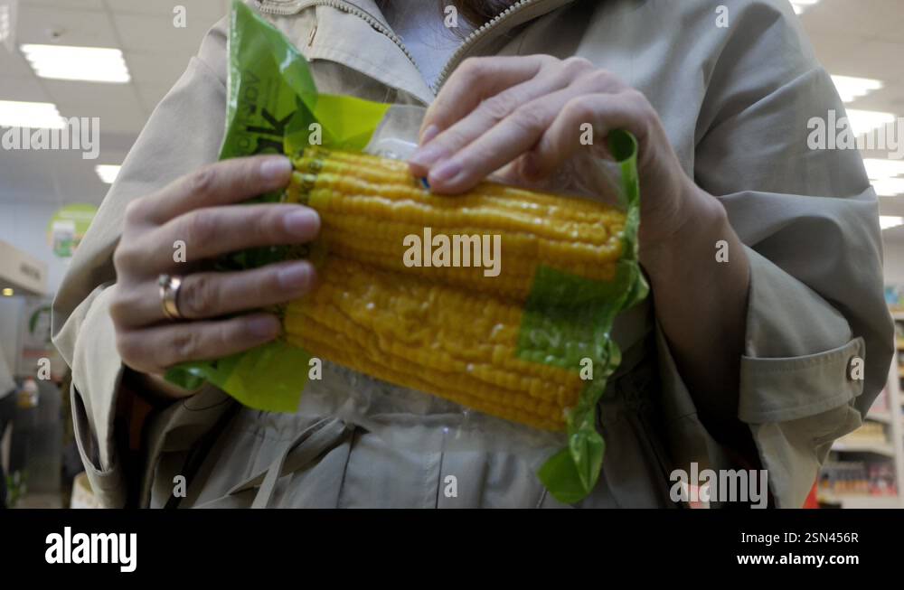 Close-up buyer woman buying corn on the cob in plastic packaging. Food ...