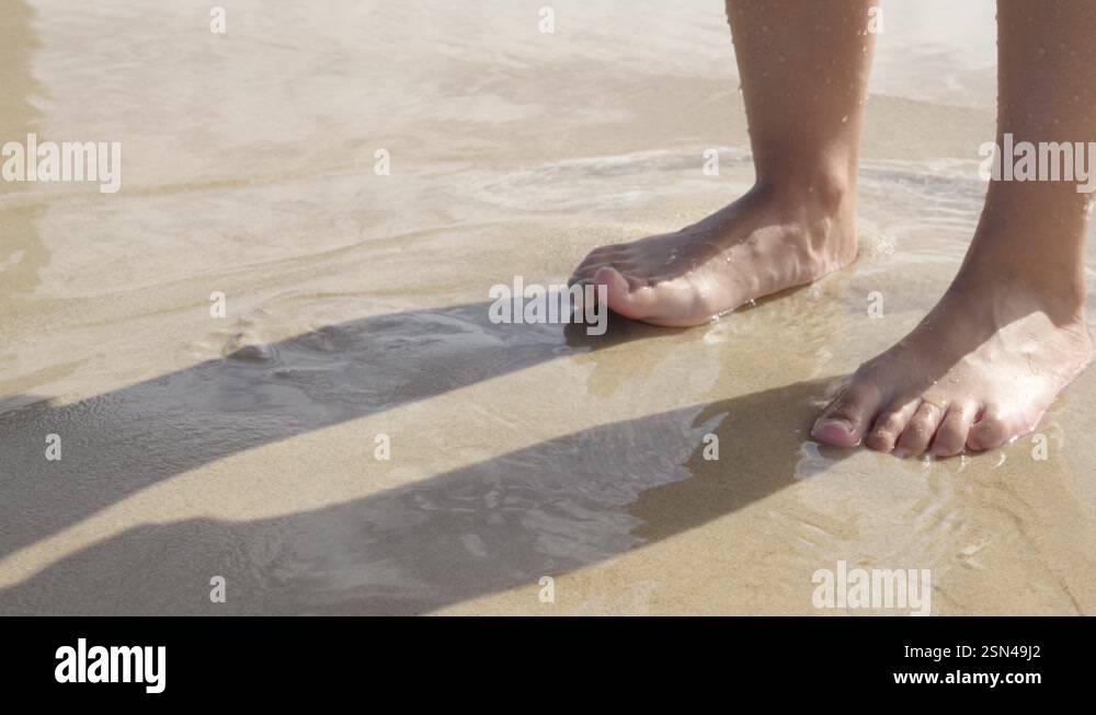 Feet in wet sand on the beach, up-close barefoot female woman legs foot ...