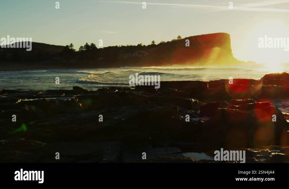 Golden hour glow of light cast across overlook peak and rocky shoreline ...