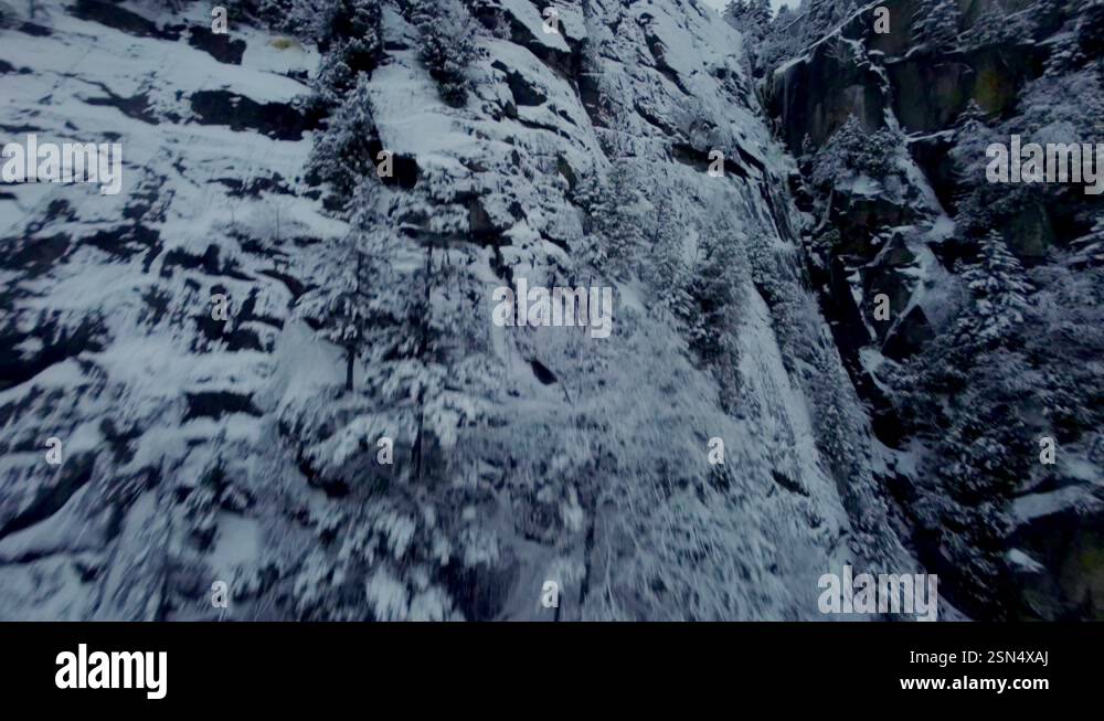 FPV drone glides along a rocky snow-covered trail, highlighting a steep ...