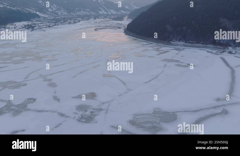 A frozen lake with cracks and snow-covered patches seen from above in ...