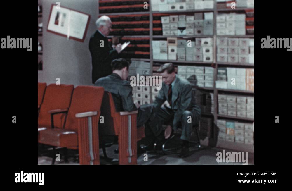 1940s: shoe store clerk sits, puts shoe on customer with shoehorn ...