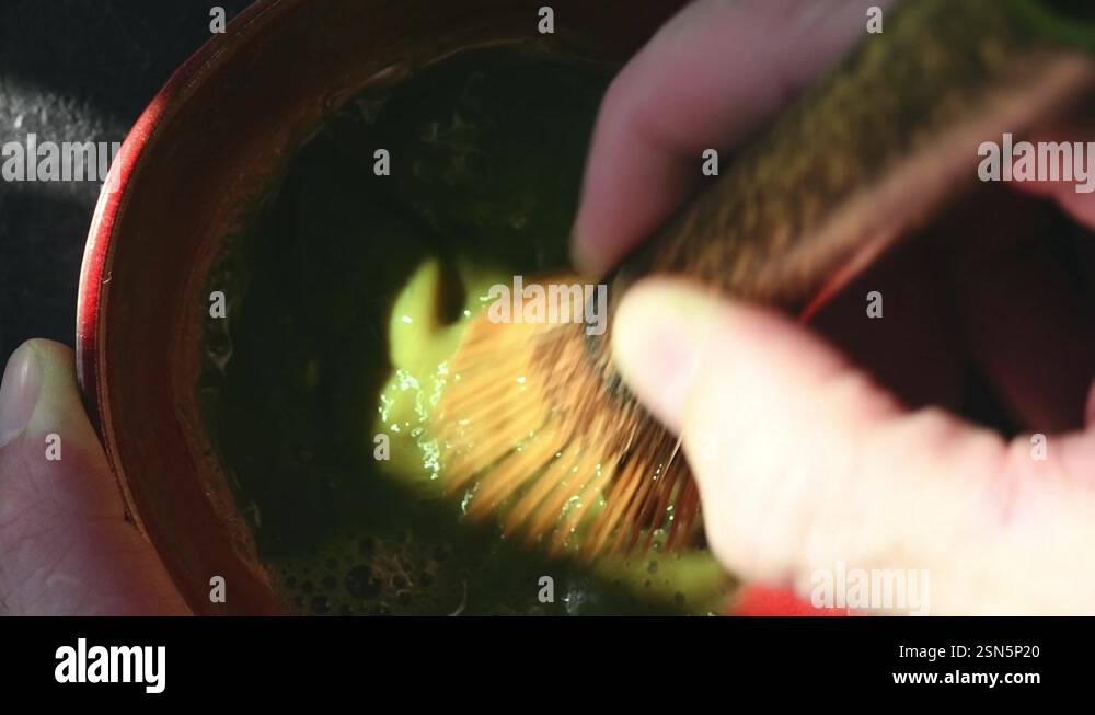 Close-up video of a bamboo whisk mixing matcha green tea powder against ...