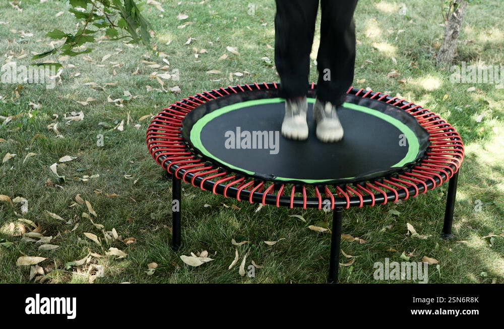 rebounding on a mini trampoline in a backyard - jumping feet and legs ...