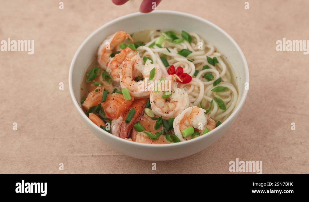 Asian dish with broth, noodles, tiger shrimp, fish and green onions ...