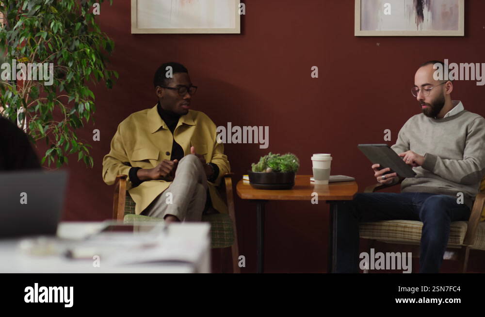 Two Multi-ethnic Young Men in Armchairs Chatting during Workday Stock ...