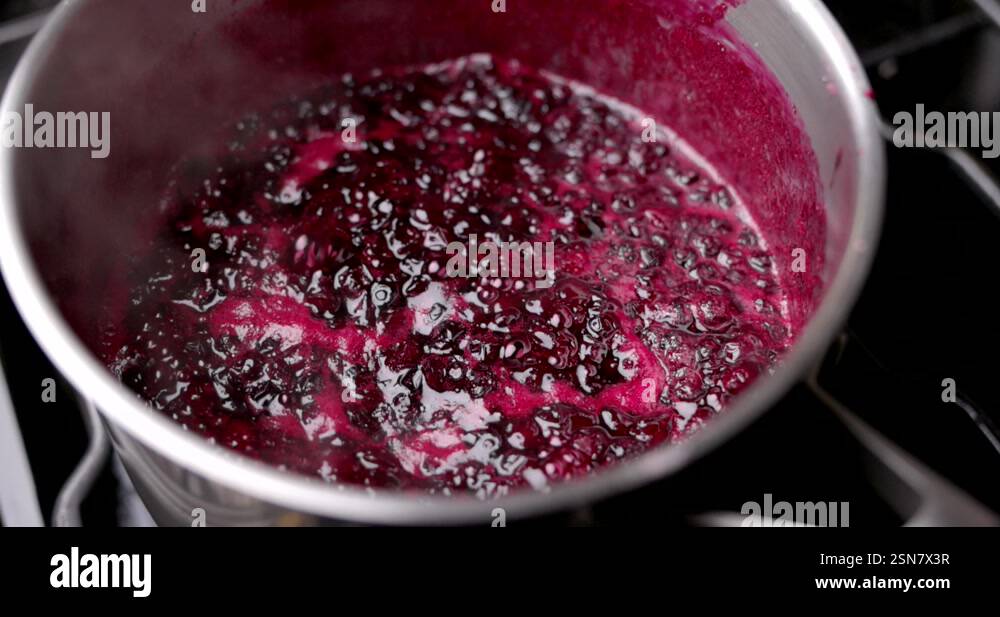 A pot of purple huckleberries is boiling on a stove making fresh jam ...