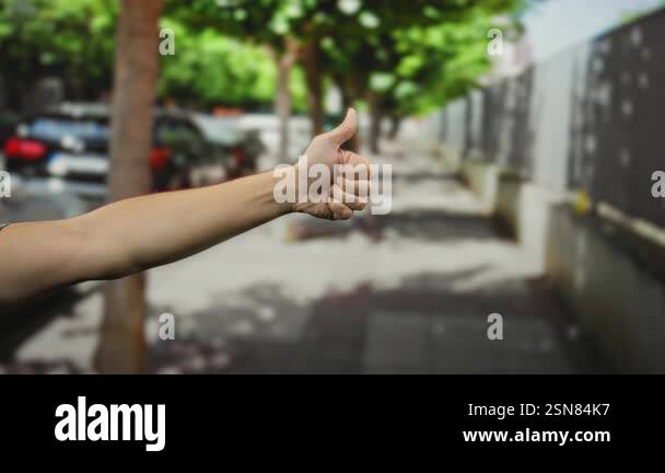 Man's hand making a thumbs-up gesture on a city street with blurred ...