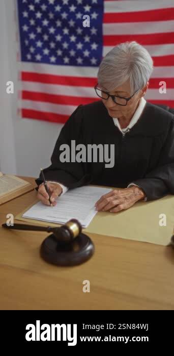 Female judge with grey hair and glasses writing in a courtroom with the ...