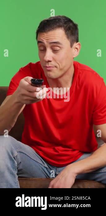 Man sitting on couch with tv remote control, flipping channels with frustrated expression ...