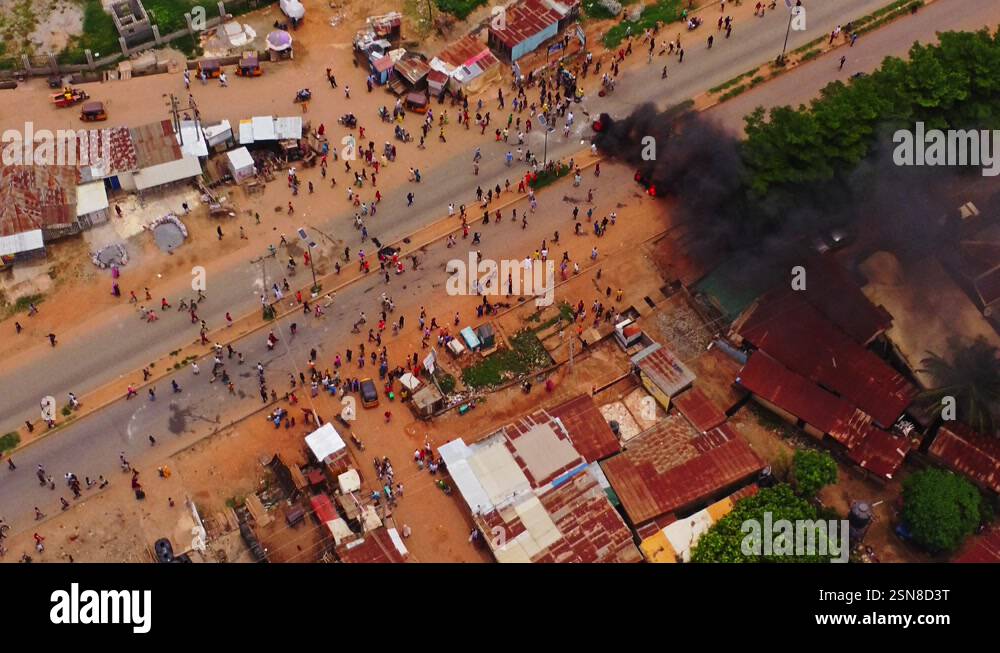 Jib up of a crowd of people walking over a street in the slums of Abuja ...