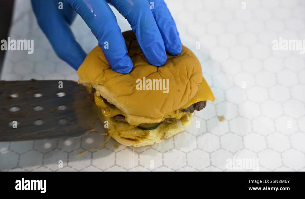 4K slow motion of a chef places the top half of a double cheeseburger ...