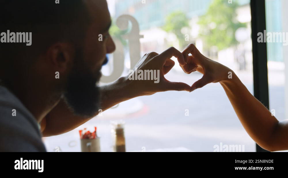 Side view of young Biracial couple forming heart shape with hands in ...