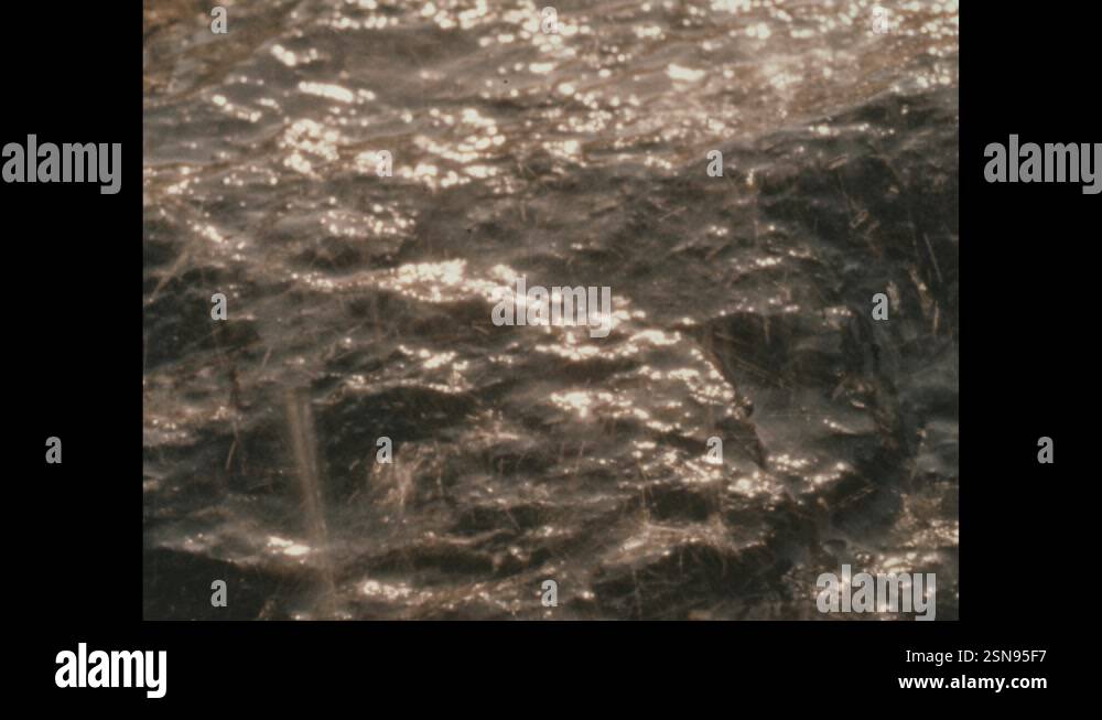 1960s: raindrops fall and splash on wet rock with sunlight glinting off ...