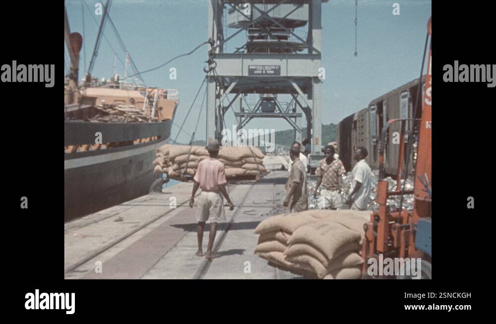 1960s: Workers adjusts ropes on pallet of sacks near cargo ship and ...