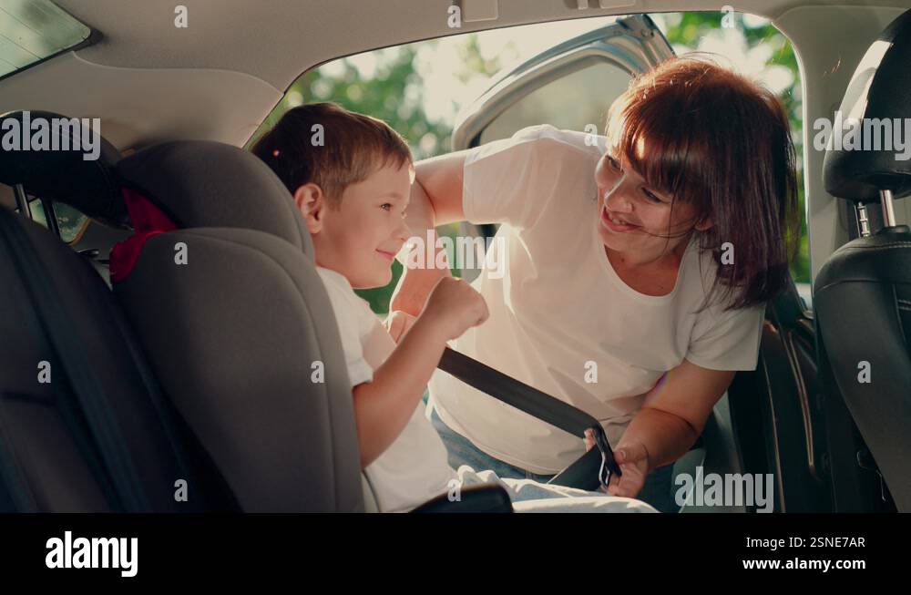 Mother secures her son in car seat using child safety belt. Family road ...