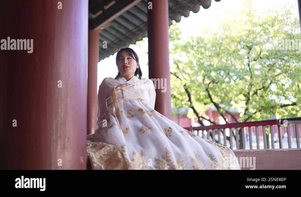 Korean female in her 20s wearing hanbok and sitting in a historical ...