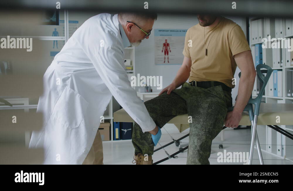Doctor Examining Broken Leg of Soldier, Sitting on Medical Couch with ...