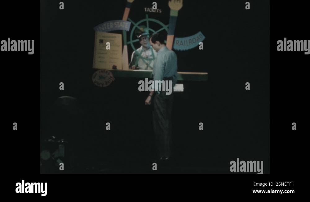 1950s: Man talks with man behind ticket window for railroad, pointing ...