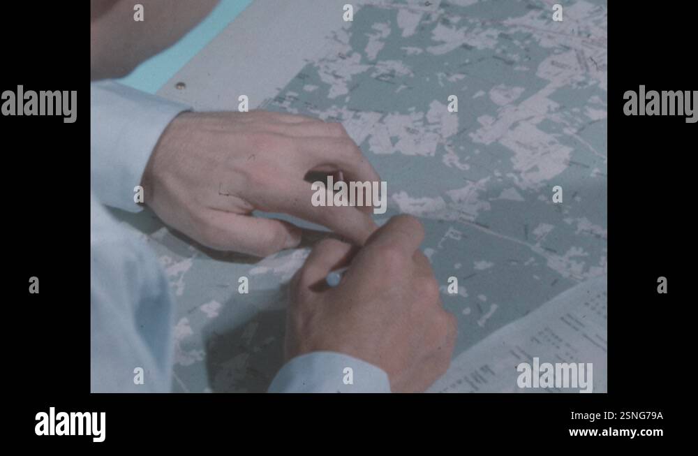 1960s: A man sits at a desk focused on a detailed topographic map. His ...