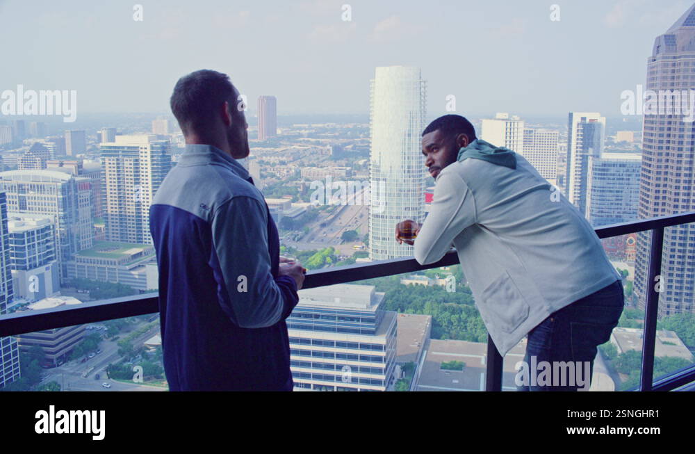 Two men lean on the railing of a luxury penthouse balcony with views of ...