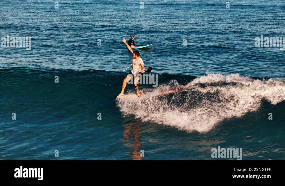 Man surfs the wave and does hand five trick by walking to the nose of ...