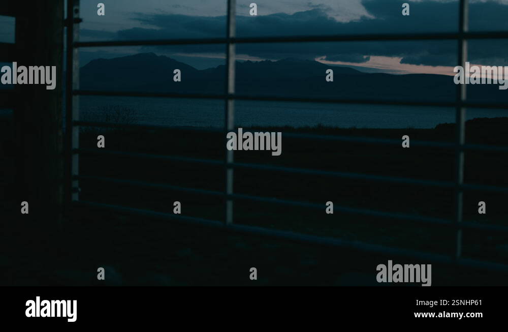 Looking through metal gate at field and distant island, in dark evening ...