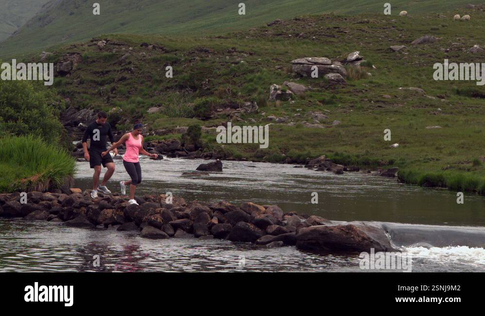 Couple crossing rocks in the middle of a flowing river Stock Video ...