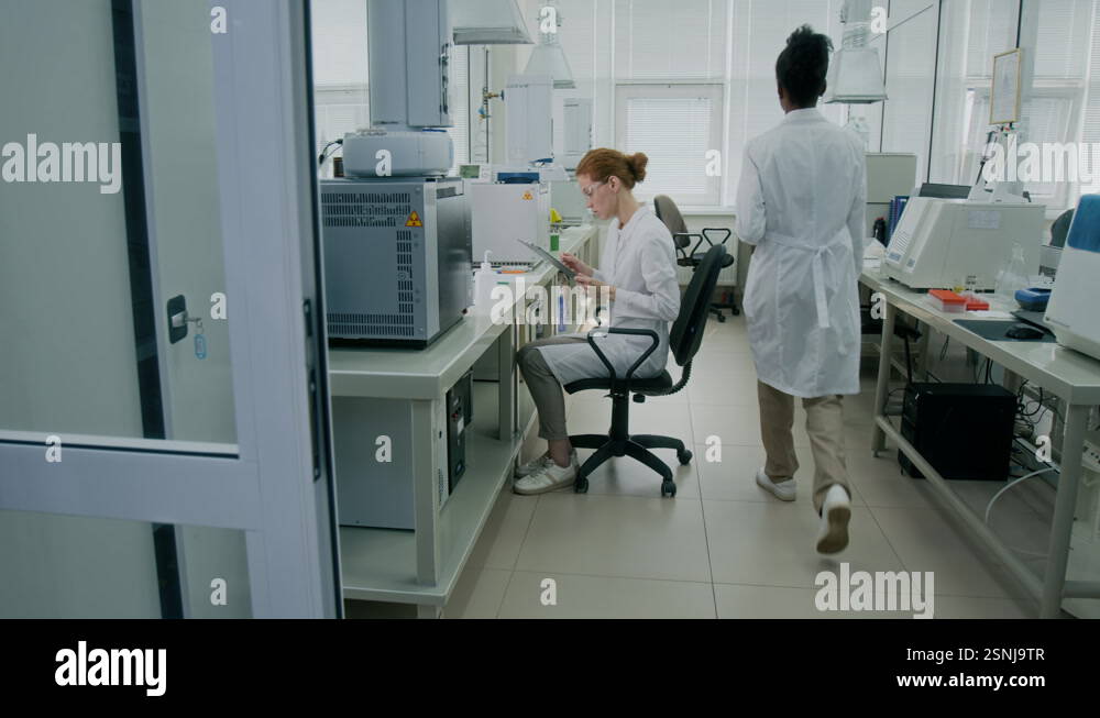 Technician Entering Laboratory, Her Coworker Studying Data on Clipboard ...