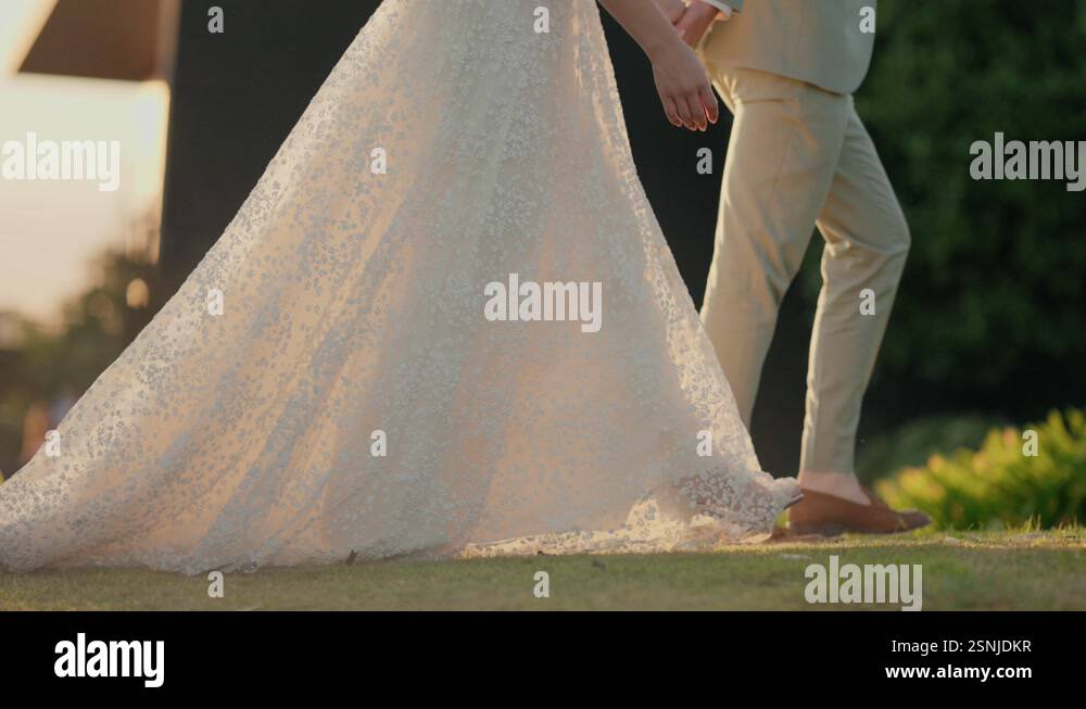 Bride and groom holding hands, walking side by side across a garden ...