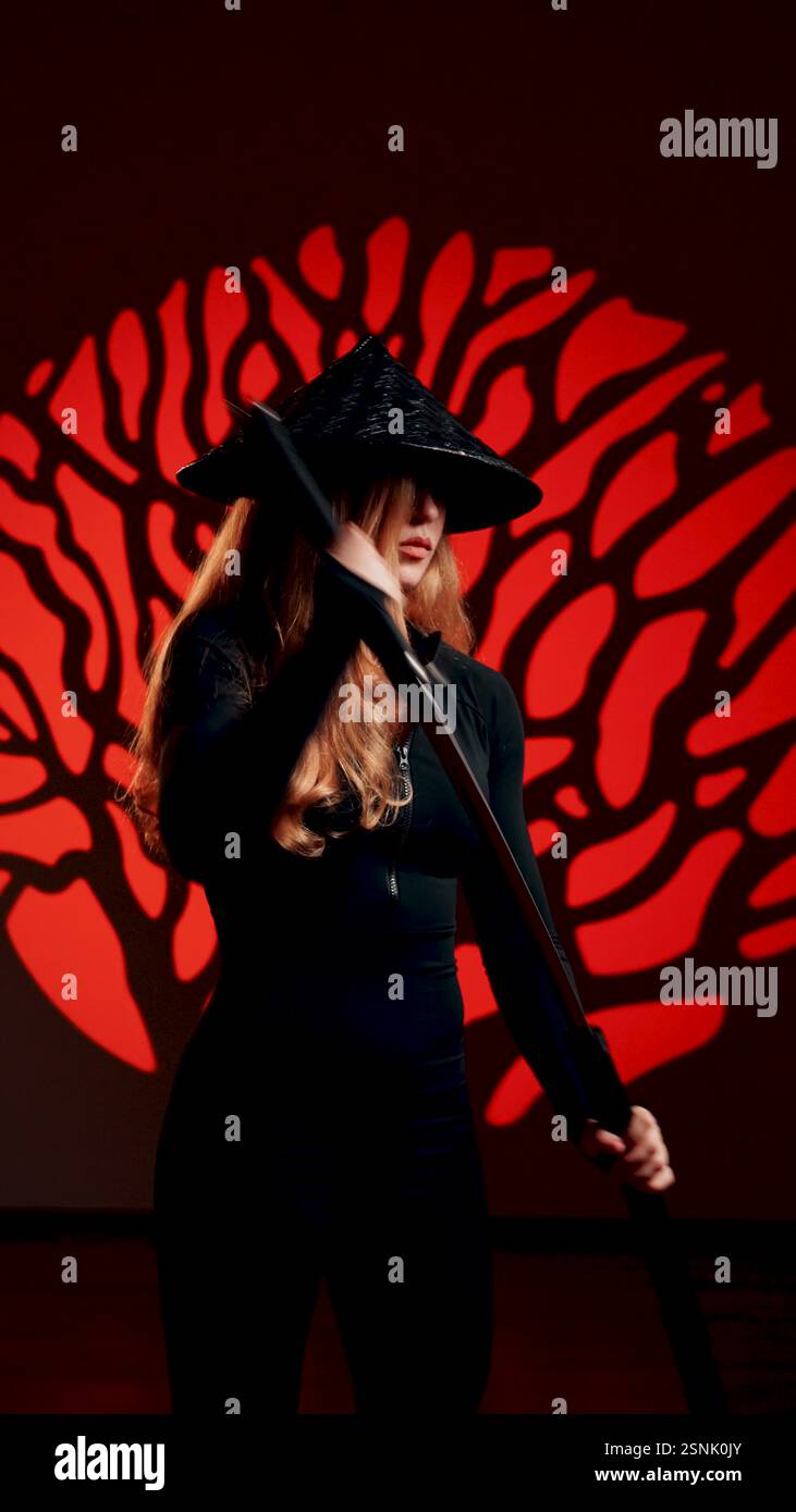 woman with a samurai sword poses against the backdrop of a light tree ...
