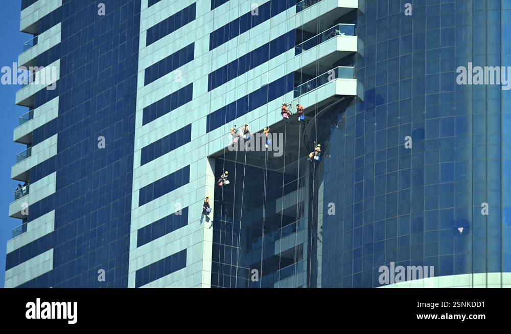 A team of workers cleaning the glass facade of a towering skyscraper in ...
