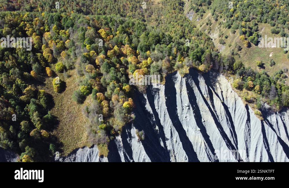 Autumn trees on rugged steep mountain slope with exposed erosion scar ...