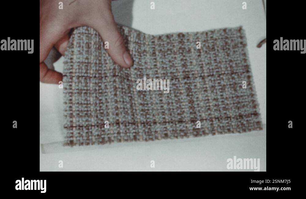 1950s: Hand tugs at swatch of homespun wool in cloth sample binder ...