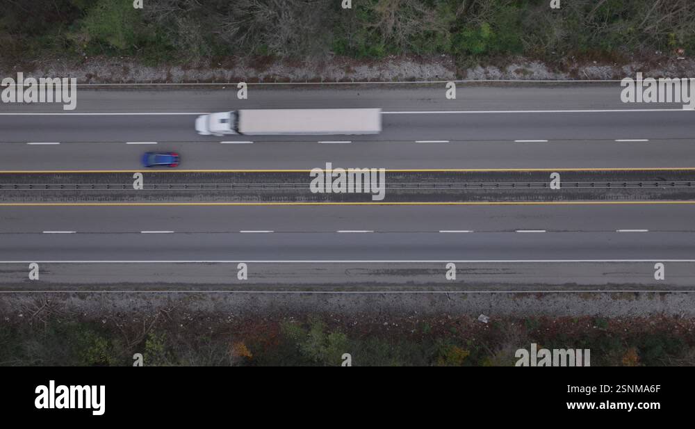 Trucks and cars drive on a highway surrounded by trees captured in an ...