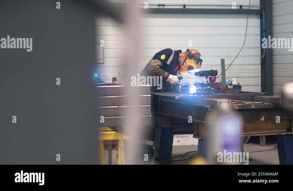 Worker welding metal on a workbench in a bright industrial workshop ...