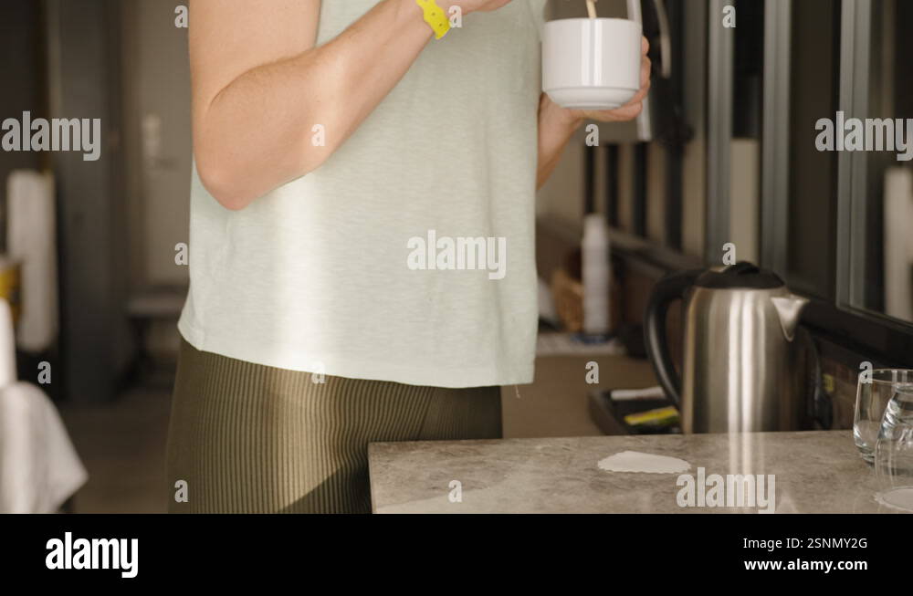 A woman stirs her drink in a white cup while standing in a modern ...