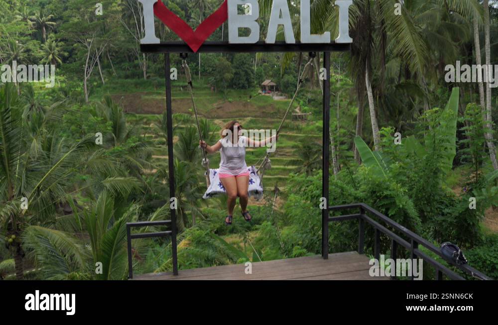 European middle aged tourist swinging under I LOVE BALI sign,rice ...