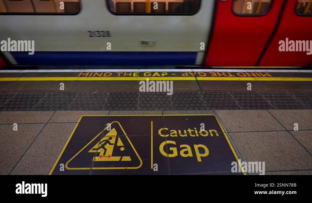 London Underground train arriving at a platform with caution signs and ...