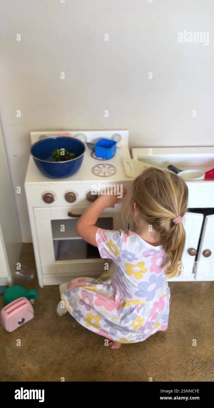 Little blonde girl play in toy kitchen turning knobs of stove and oven ...