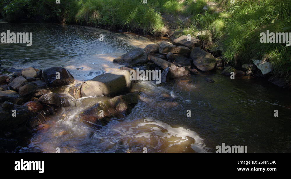 Wide shot over a small stone dam of rocks and boulders over a stream of ...