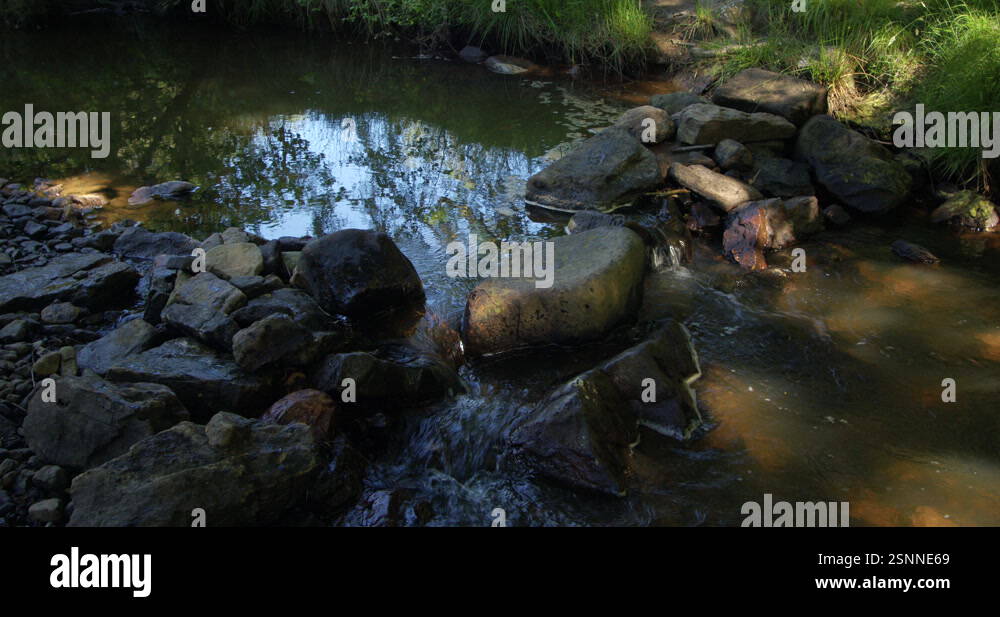 mid shot over a small stone dam of rocks and boulders over a stream of ...