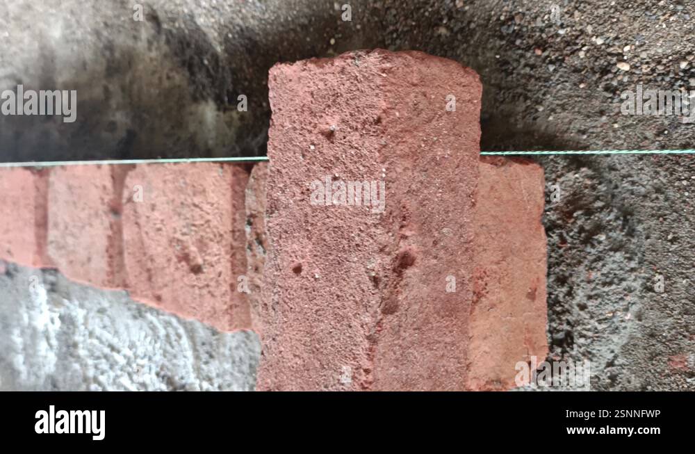 Workers at the construction site lay bricks in a straight row using a ...