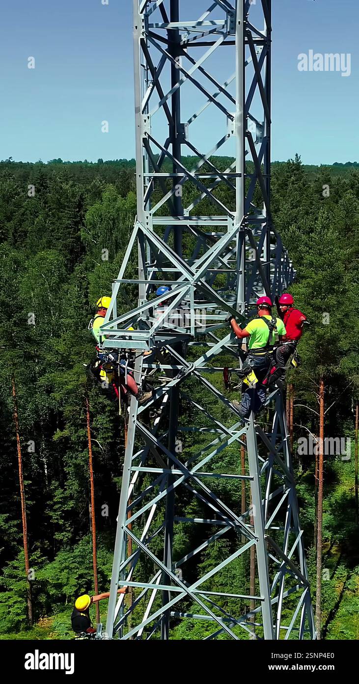 Team of workers scaling a high-voltage transmission tower in a forest ...