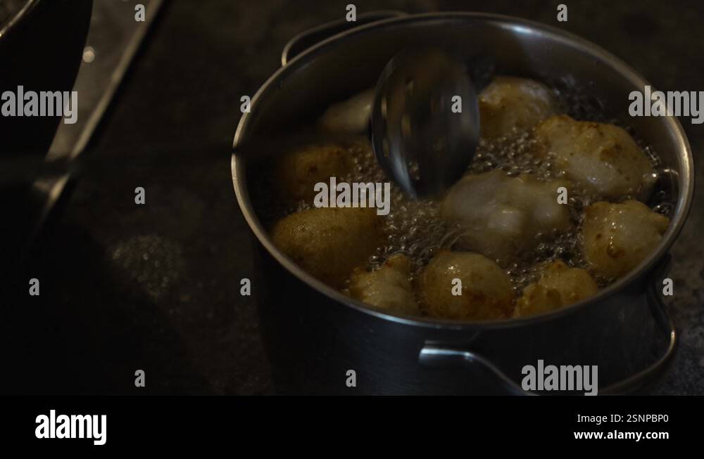A pot sizzles as round snacks are fried in hot oil, creating a golden ...