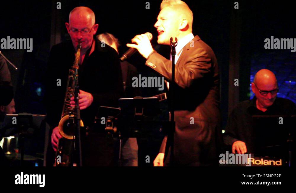 The male vocalist sings on stage with the musicians playing in the ...