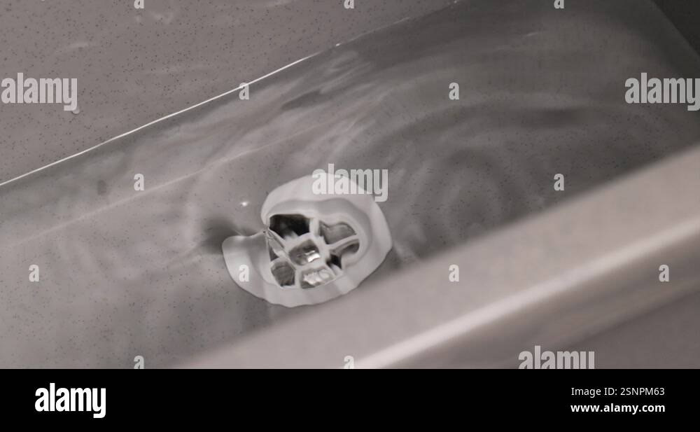 Close-up of a Caucasian male hand pulling a white plug from a grey sink ...